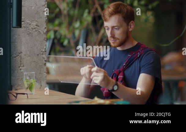 Ginger man with innovative tablet sitting in the cafe, using ...