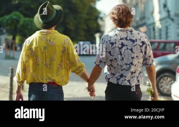 Shot back young gay couple hold hands hug each other walk at street ...