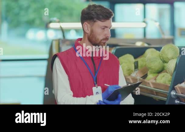 Serious young seller man write in notebook in supermarket check ...