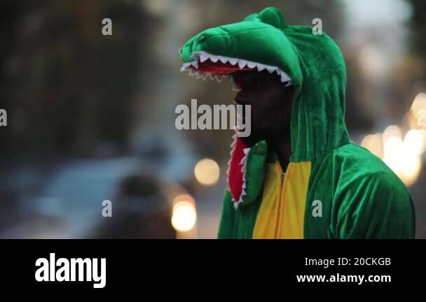 Lonely cute green dinosaur standing outdoor in busy road. Portrait of ...