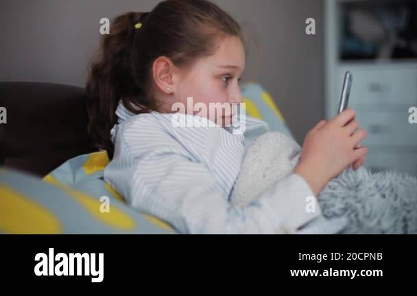 Beautiful young girl using the phone lying on the bed scared throws ...