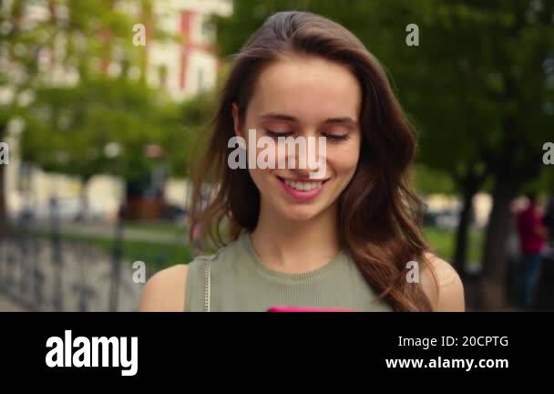 Attractive smiling young woman in a bright sunlight uses red phone walk ...