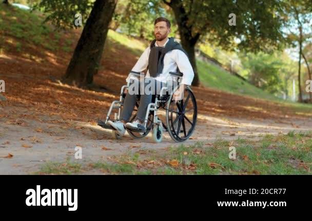 On sunny day young man disabled in wheelchair rides in park at sunlight ...