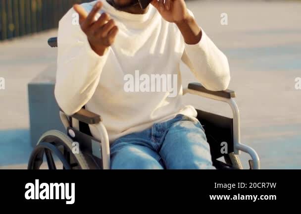 Close up face young man use speak on phone on a wheelchair in a park ...