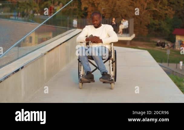 Happy young man use phone on a wheelchair read good news in a park look ...