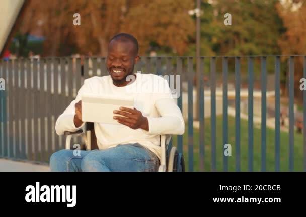 Smiling young african american man on a wheelchair with tablet computer ...