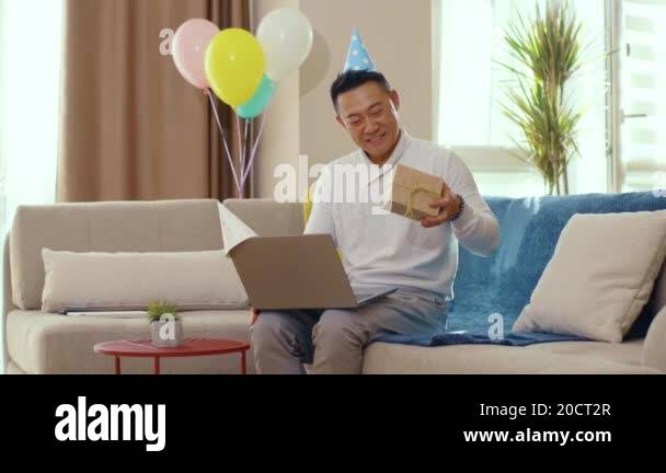 At home asian adult happy man congratulating sister with birthday party showing gift box saying ...