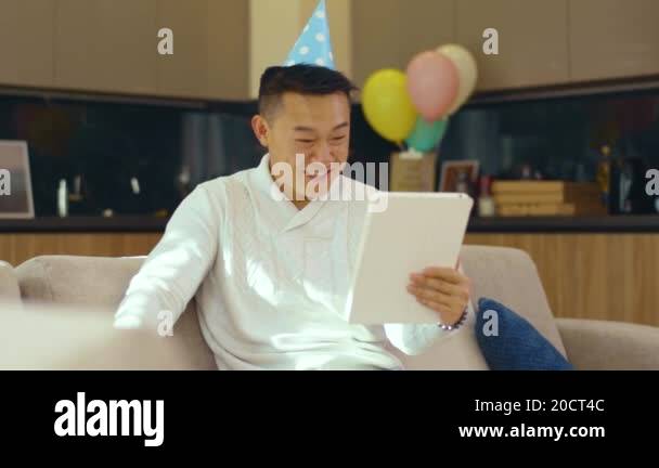 One person party. Asian man in birthday hat connecting to friends via ...