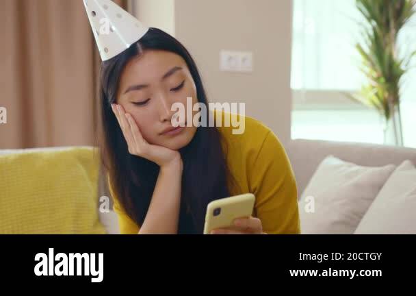 Unhappy chinese woman staying home alone for birthday taking off festive cap having no messages ...