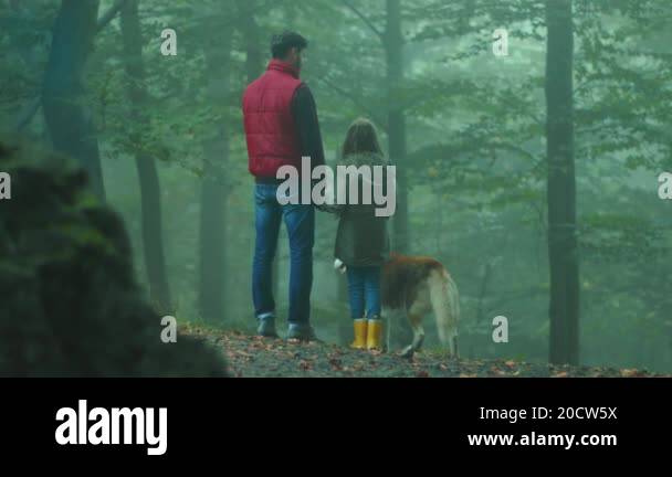 Shot back father and daughter standing in forest with dog at autumn weekend communicating ...