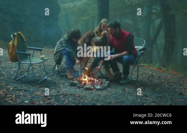 Family with dog sit around a campfire on autumn evening in the woods ...