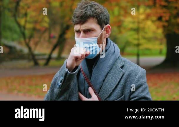 Sick young man with sad face and a protective mask coughs stand in ...