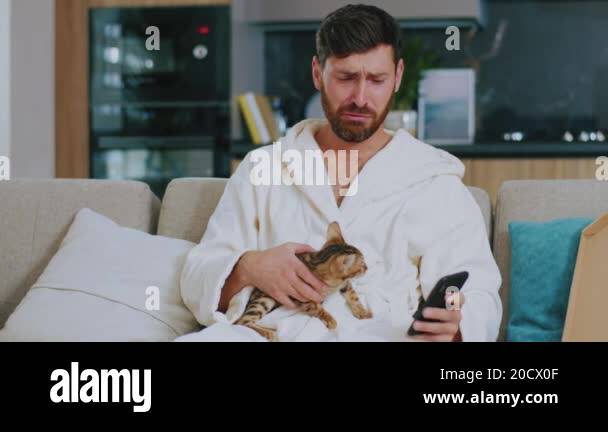 Close up crying sensitive man with cat use phone watching TV. Sitting ...