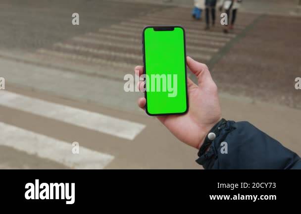 Close up man hand using and tapping phone with vertical green screen on blurred background ...