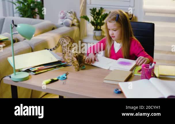 Funny child girl learning writing doing homework sitting at home table ...