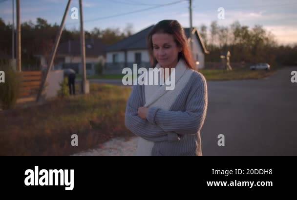 Woman walking on a quiet rural street, arms crossed, smiling gently ...