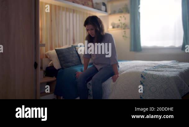 Woman sitting on bed, curled up in sorrow, gripping her knees while ...
