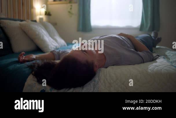 Woman lying on bed staring upwards, appearing emotionally exhausted and ...