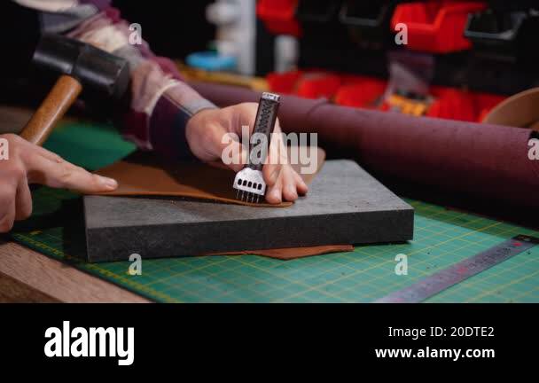 A craftsman carefully punches stitching holes into leather for shoe ...
