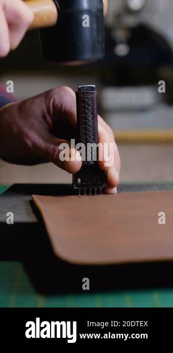 A craftsman punches stitching holes into leather with a mallet and ...