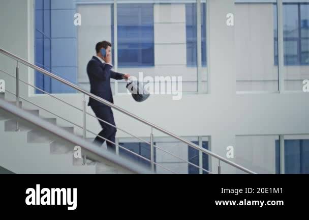 Man descending office stairs speaking cellphone checking wristwatch ...