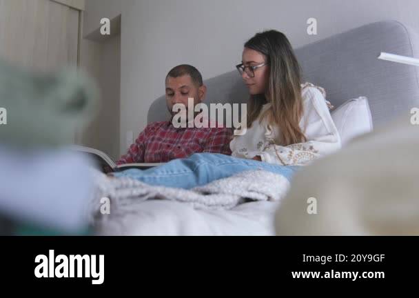 A man and woman are sitting on a bed with a magazine open in front of ...