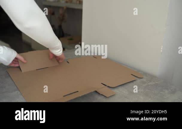 A video showcasing female hands assembling a kraft cardboard self-assembly box on a textured ...
