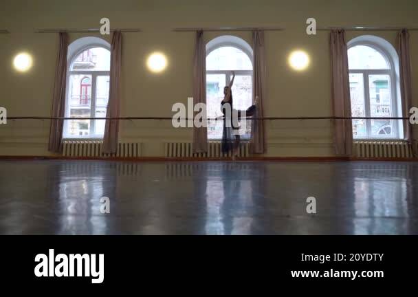 Prima ballerina in white skirt and pointe stretching practicing ballet ...