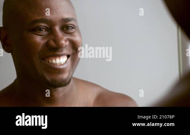 African American man in his 30s smiles at his reflection in the mirror ...