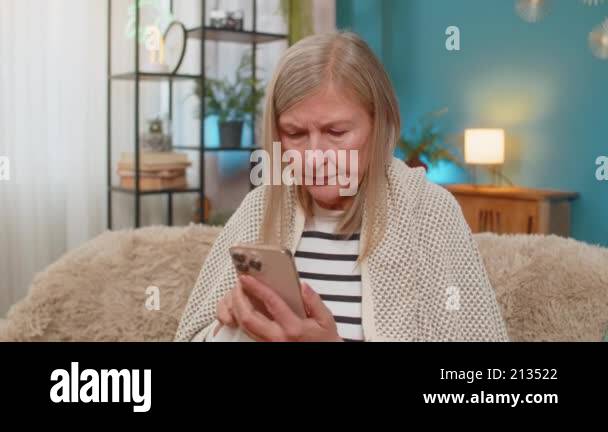 Caucasian ill mature woman sits on home sofa covered with blanket ...