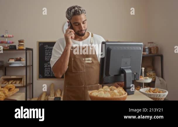 Young man with a beard working in a bakery shop using a computer while ...