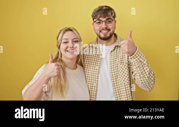 Beautiful couple showing thumb up, standing together on isolated yellow ...