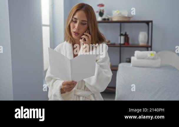 Young woman in a spa reading a brochure while talking on the phone in a ...