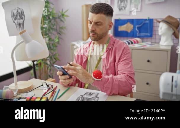 A focused man designing in a tailor shop with cellphone, sketch, sewing ...