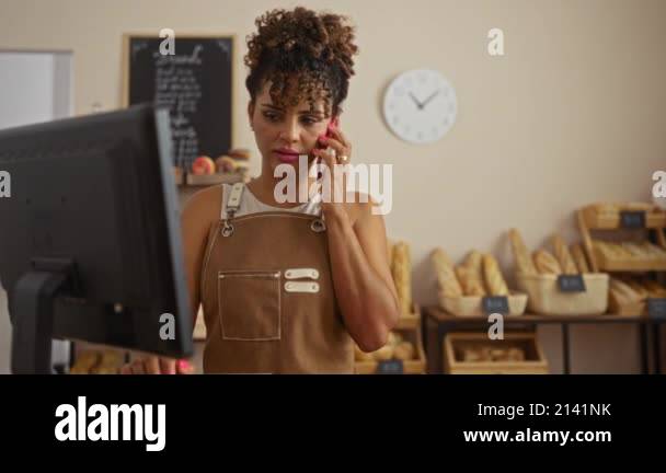 Woman working in a bakery while talking on phone near a computer ...