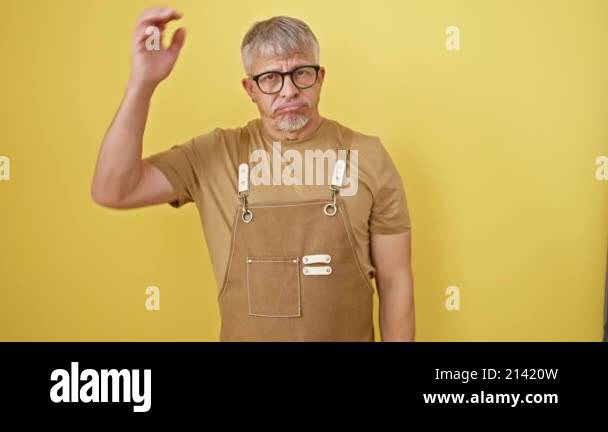 Uncertain grey-haired man in glasses and apron, pensive and full of ...