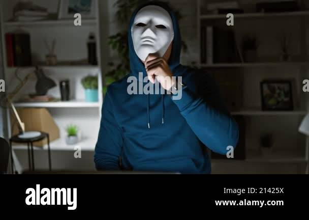 A young man wearing a mask and hoodie sitting in a modern office with a ...