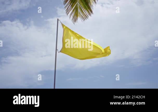 Yellow flag waving in the daylight against a partly cloudy blue sky ...