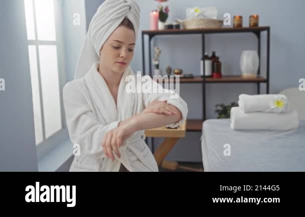 Woman applying cream in a spa setting with candles, flowers, and towels ...