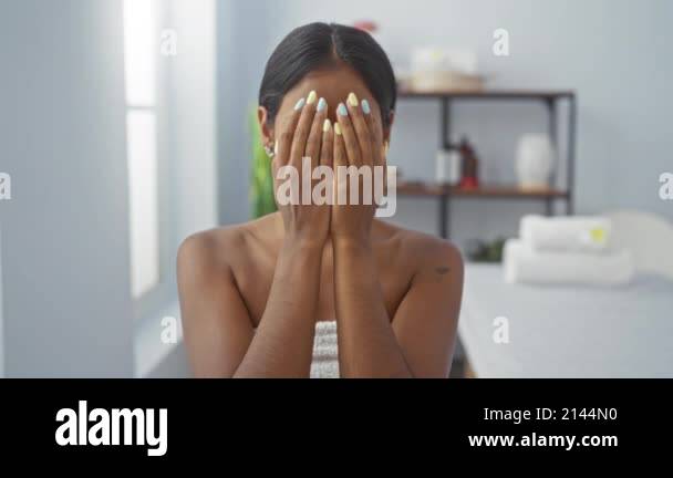 Young woman smiles as she uncovers her face with her hands in an indoor ...