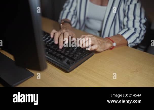 Elderly woman typing on keyboard at office desk indoors showcasing mature hands and workplace ...