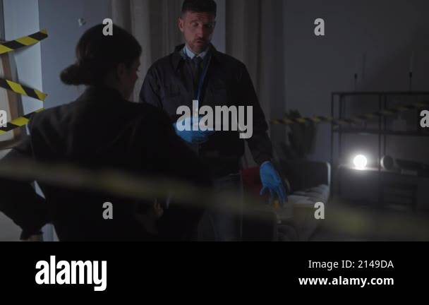 Man and woman investigators in a dark indoor crime scene discussing ...