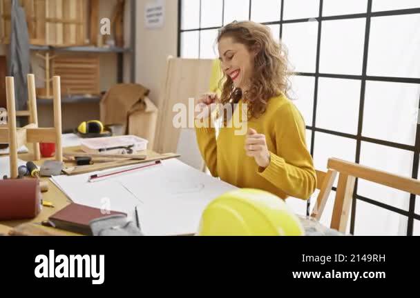 Joyful young woman celebrates her win, sitting at a carpentry table ...