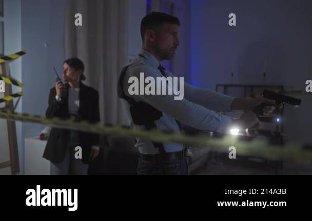 Investigators, a man and woman, search a dimly lit indoor crime scene ...