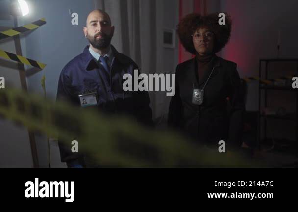 A man and woman, depicted as detectives, observe a taped-off indoor ...