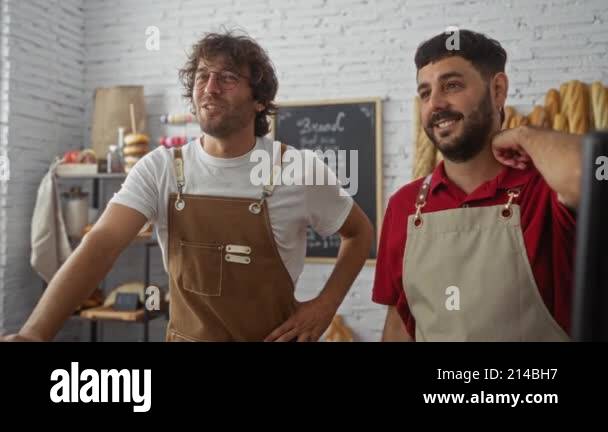 Men working together as bakers in a bakery shop, wearing aprons and ...