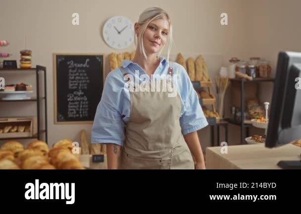Blonde woman working in a bakery stands confidently behind the counter ...