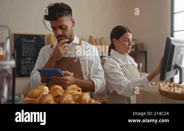 Man and woman working together in a bakery, managing tasks on tablet ...