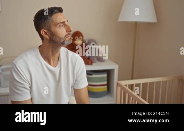 Man sitting in bedroom near baby cradle with soft toys visible in ...