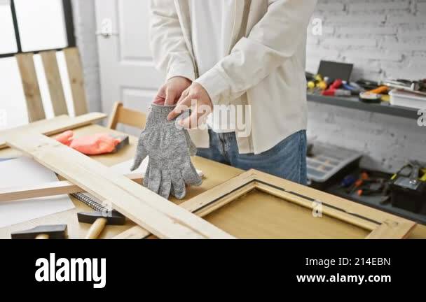 A man in casual wear puts on gloves in a well-equipped carpentry ...